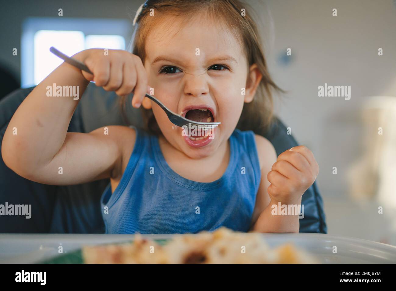 A baby girl sitting in a high chair feeding herself with a dirty face ...