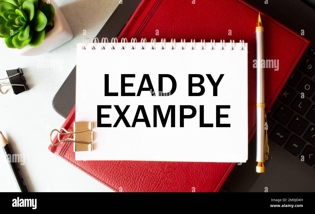Text LEAD BY EXAMPLE on Office desk table with keyboard, notepad and analysis chart on a white ...