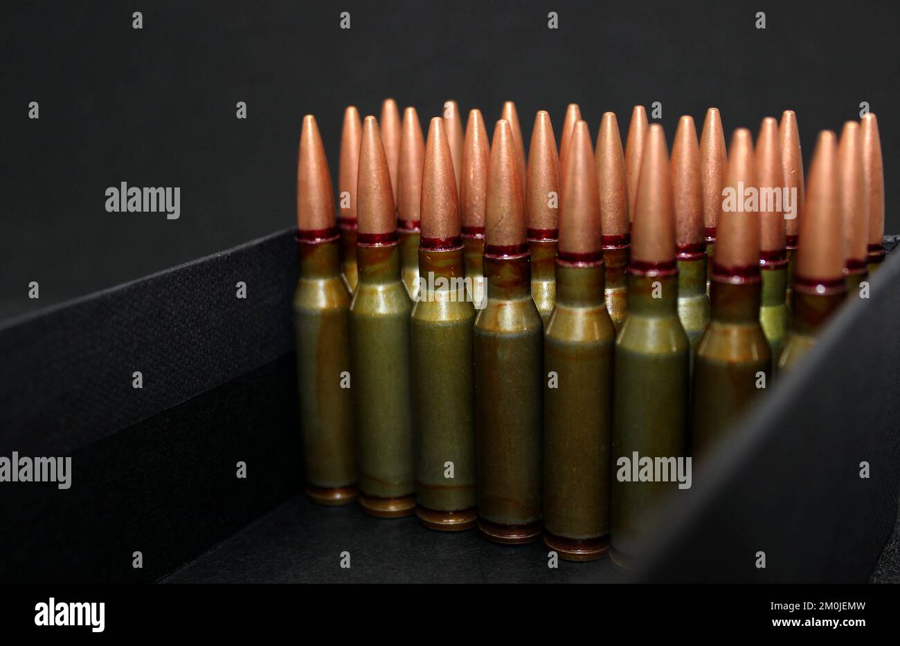 Live ammunition with copper bullets lined up in even rows in a black ...