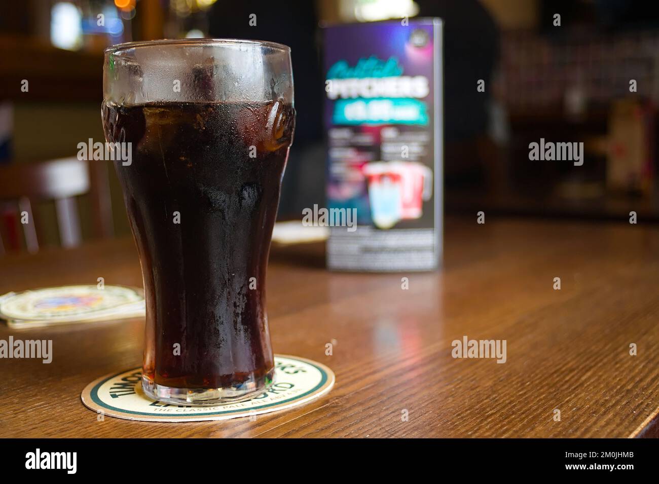 A large glass of cola on a tabletop in a UK pub with defocused ...
