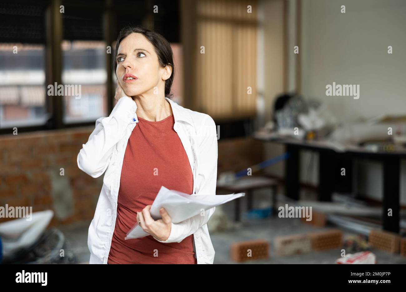Confused woman standing with papers in apartment during renovations ...