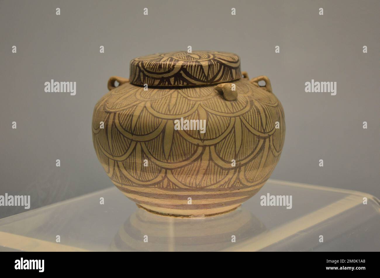 An ancient earthenware jar displayed in a museum with simple circular ...