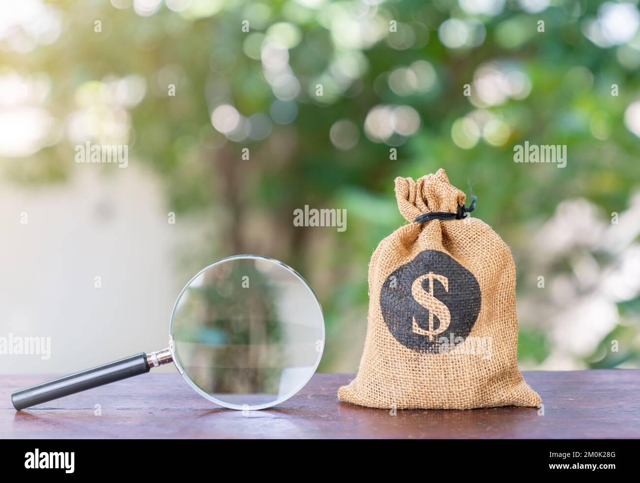 Budget and savings concept. Magnifying glass next to a bag of money on ...