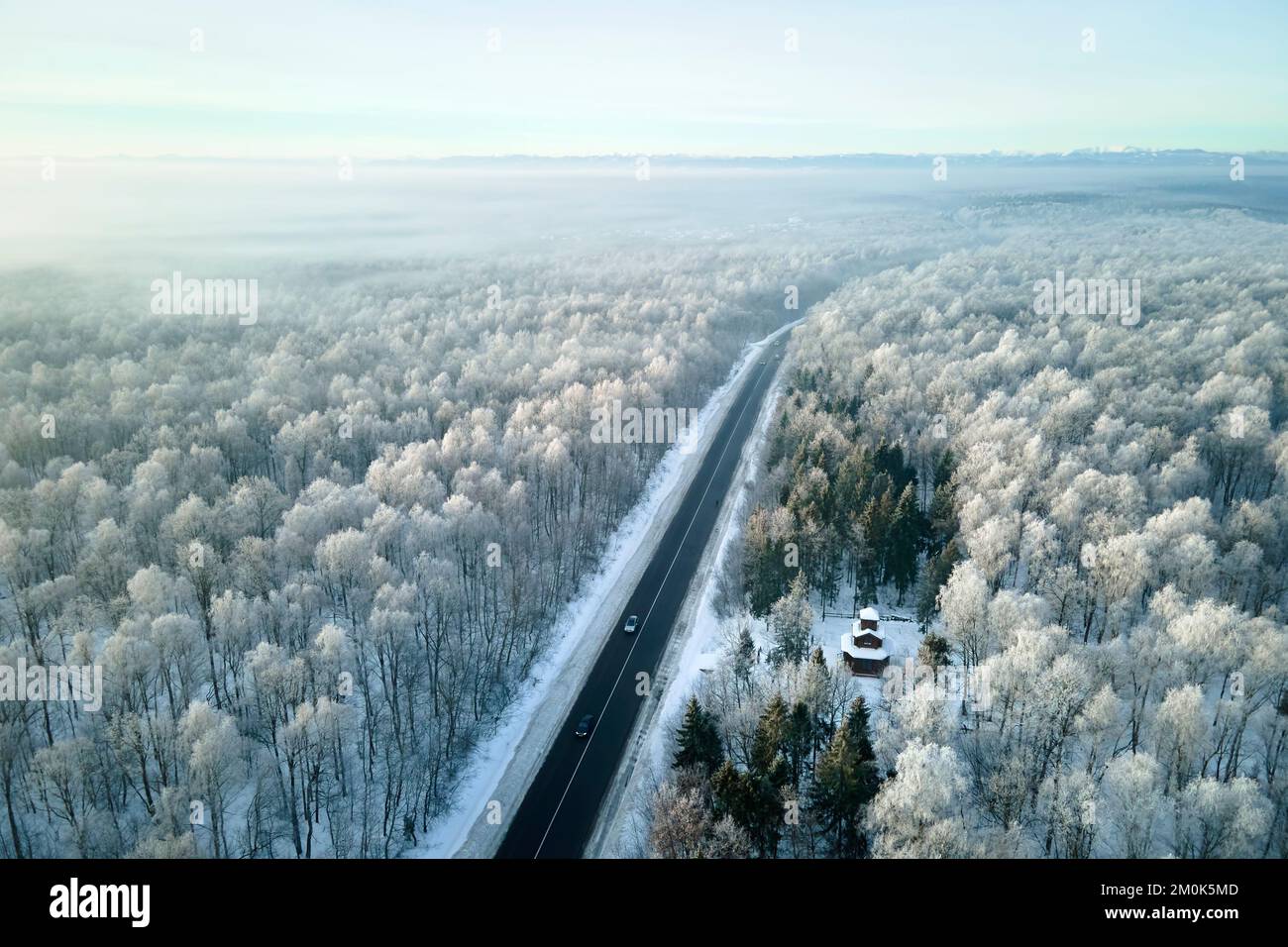 Aerial view of winter landscape with snow covered woods and black asphalt forest road on cold ...
