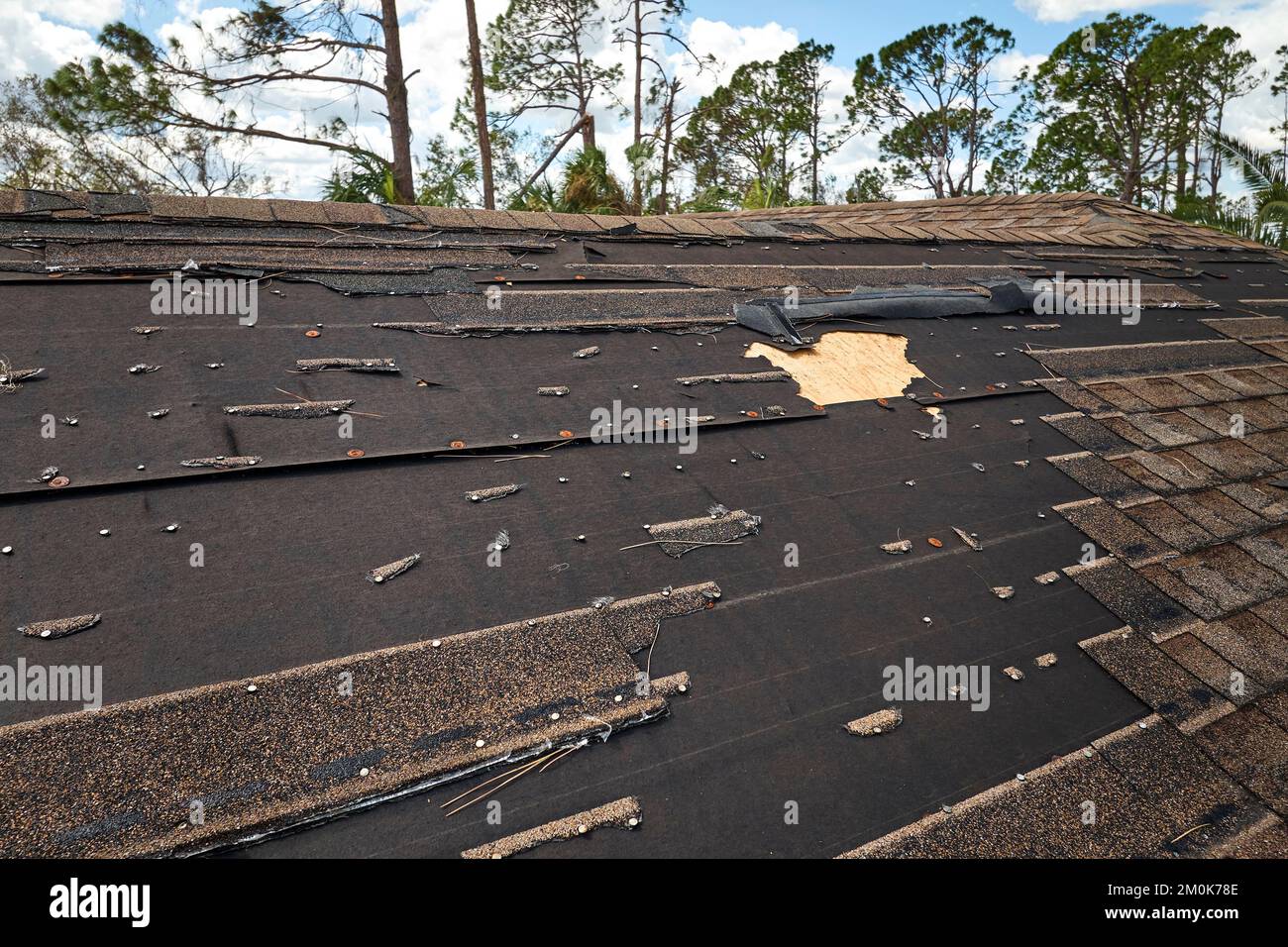 Wind damaged house roof with missing asphalt shingles after hurricane ...