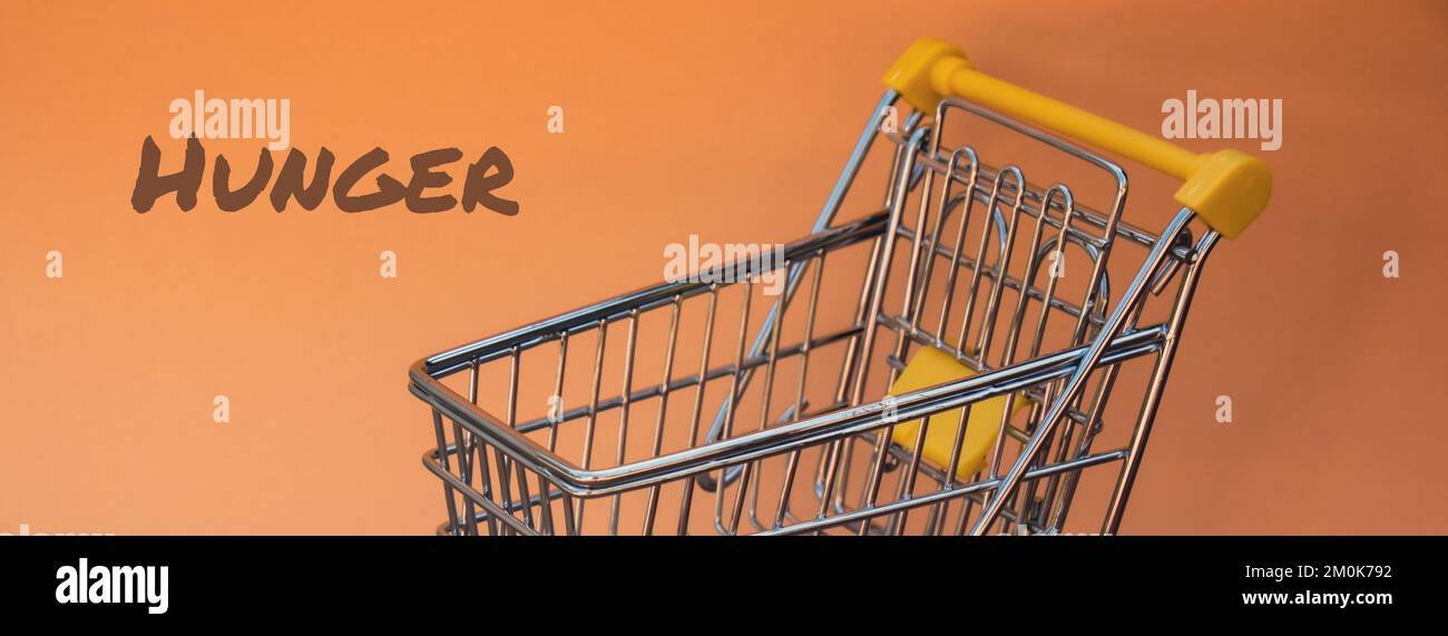 HUNGER text against Empty shopping trolley cart on beige background ...