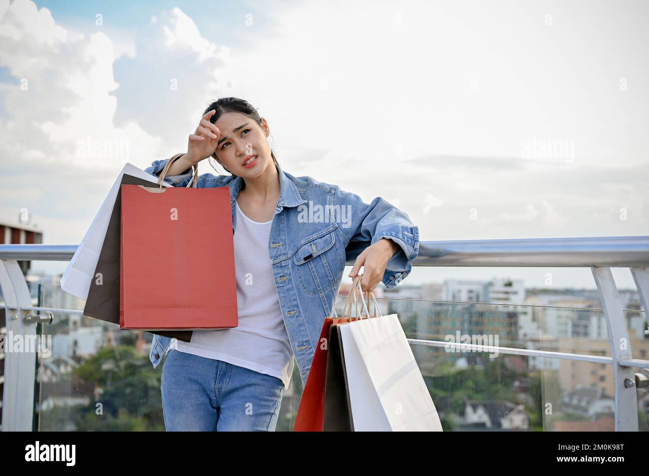 Exhausted and tired young Asian woman carrying her shopping bags on a ...