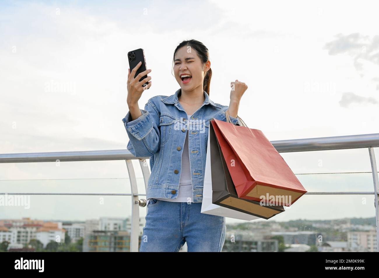 Asian woman using smartphone while carrying shopping bags, enjoys ...