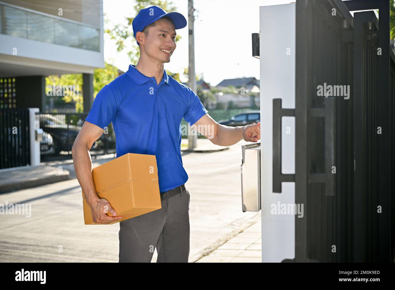 Asian delivery man in blue uniform ringing the doorbell in front of ...