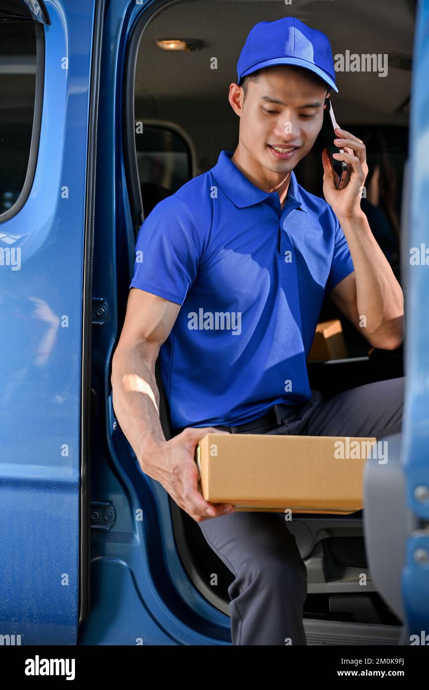Asian delivery man in blue uniform calling his customer before giving ...