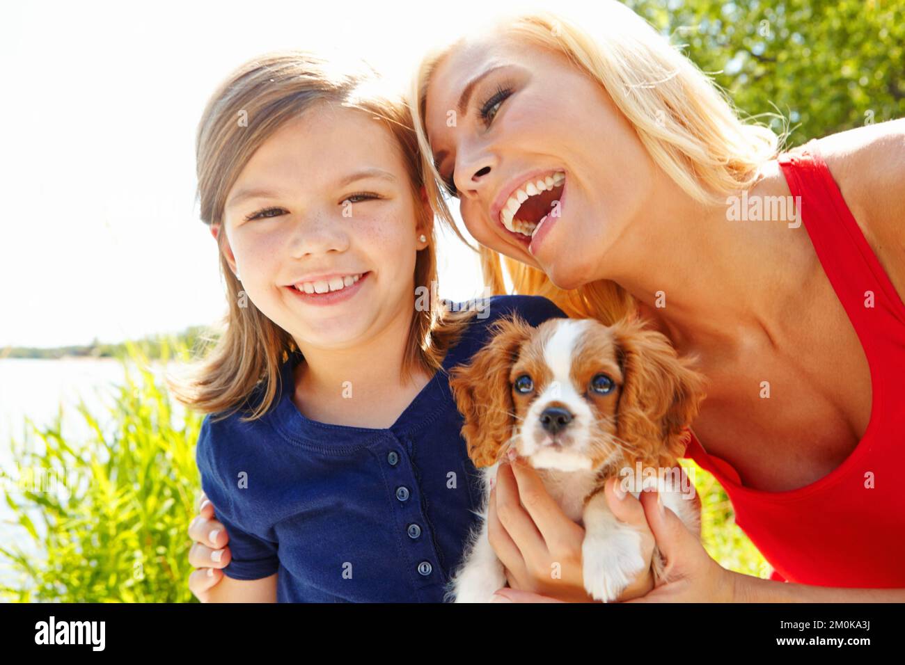 Moms the best. Portrait of a little girl holding a puppy while her mother smiles at her lovingly ...