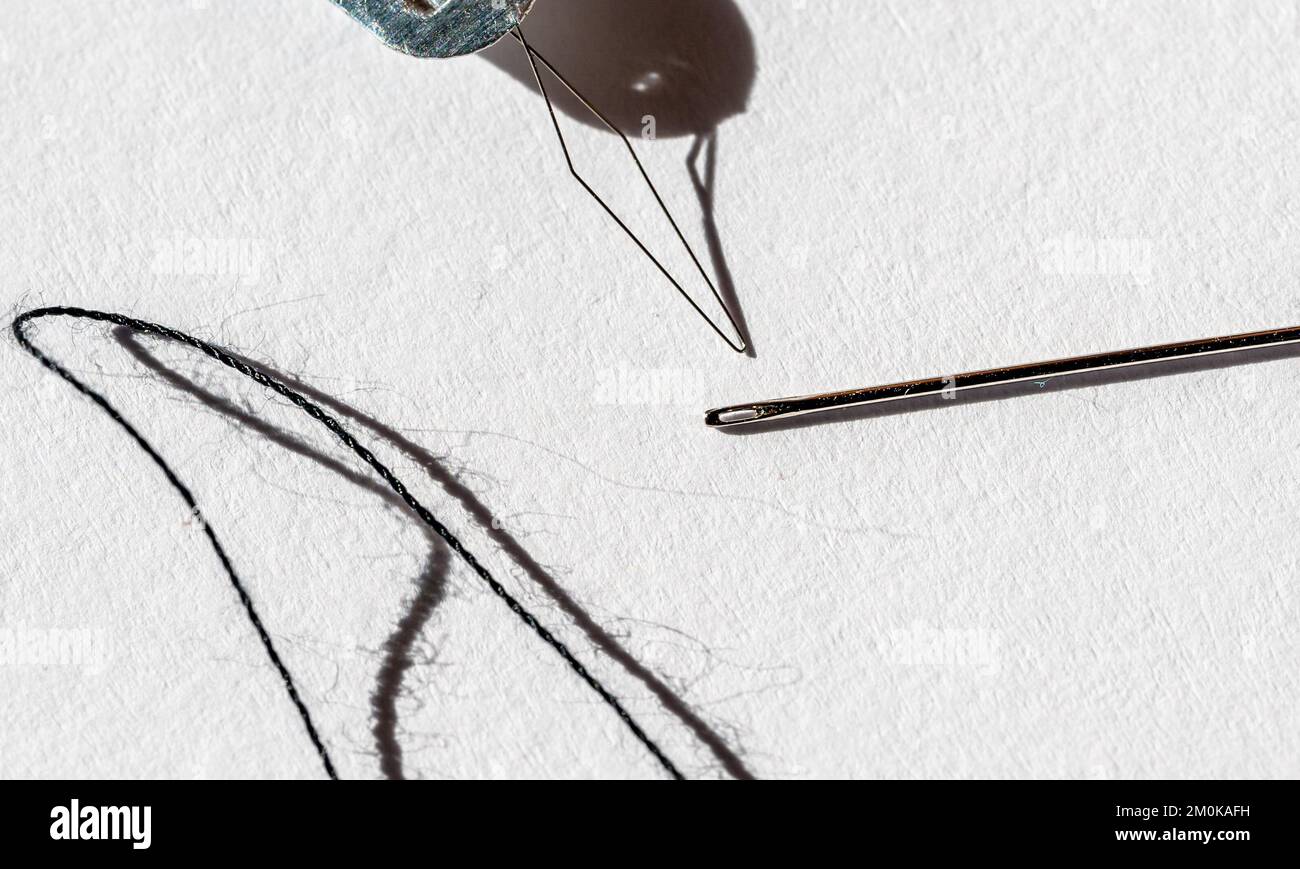 Sewing needle threader tool in use and a single black string Stock ...