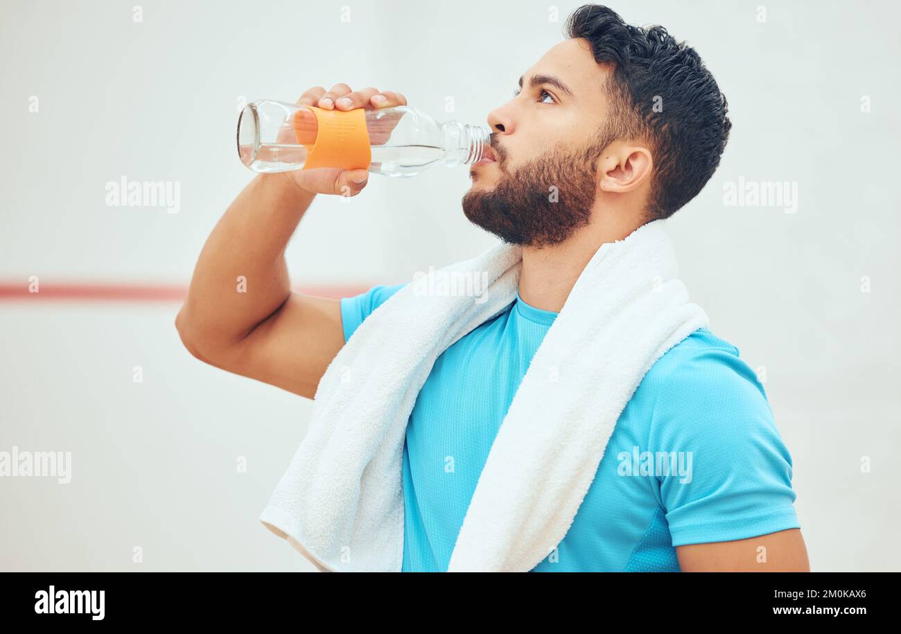 Young athletic squash player standing alone and drinking water after ...