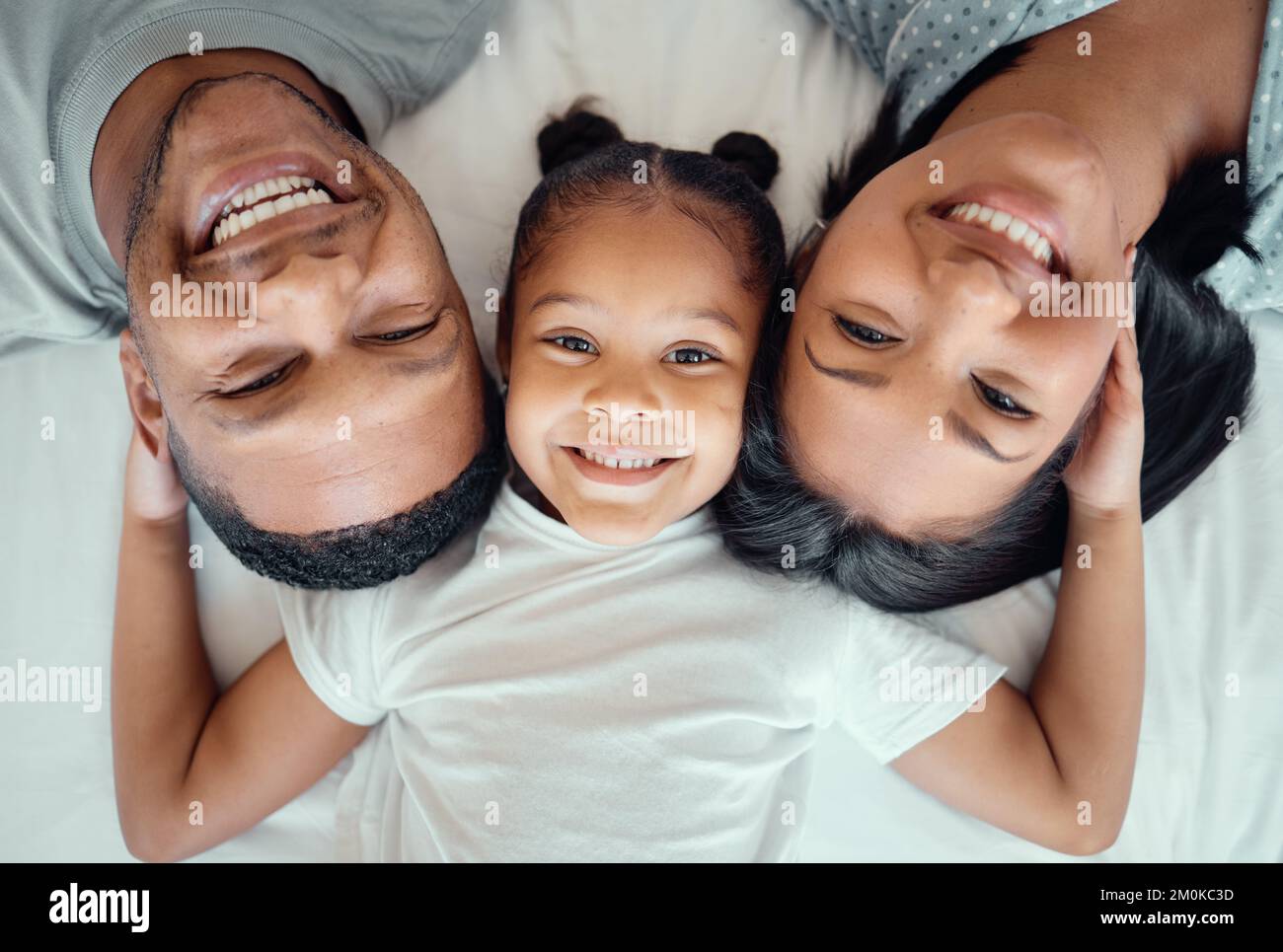 Adorable little girl pulling her parents close while lying in between ...