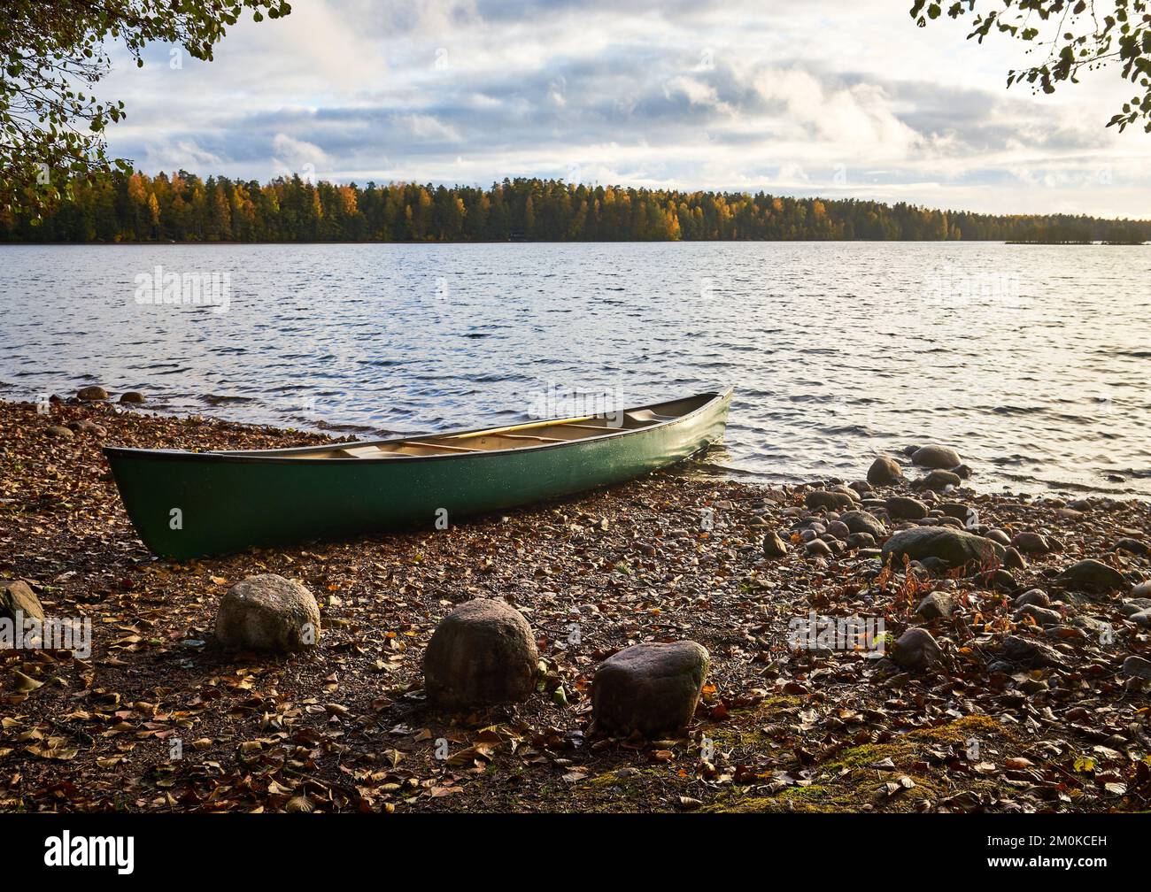A small green canoe boat on dirt seaside by the sea with trees on the ...