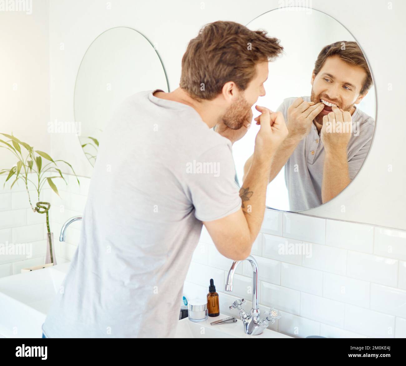 One handsome man flossing his teeth in a bathroom at home. Caucasian male using floss to prevent ...