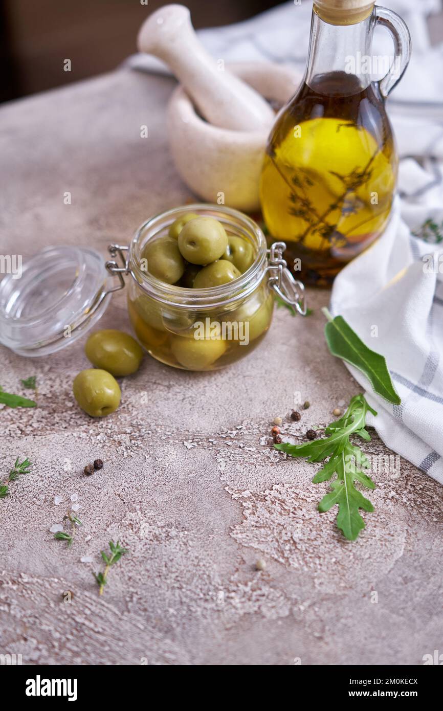Canned green olives in a glass can and small bottle of olive oil with ...