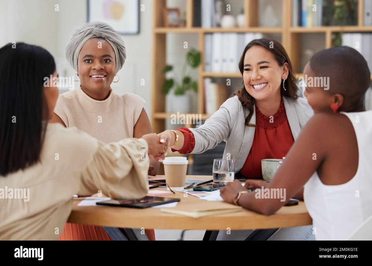 Team of smiling diverse business women shaking hands in office after meeting in boardroom. Group ...