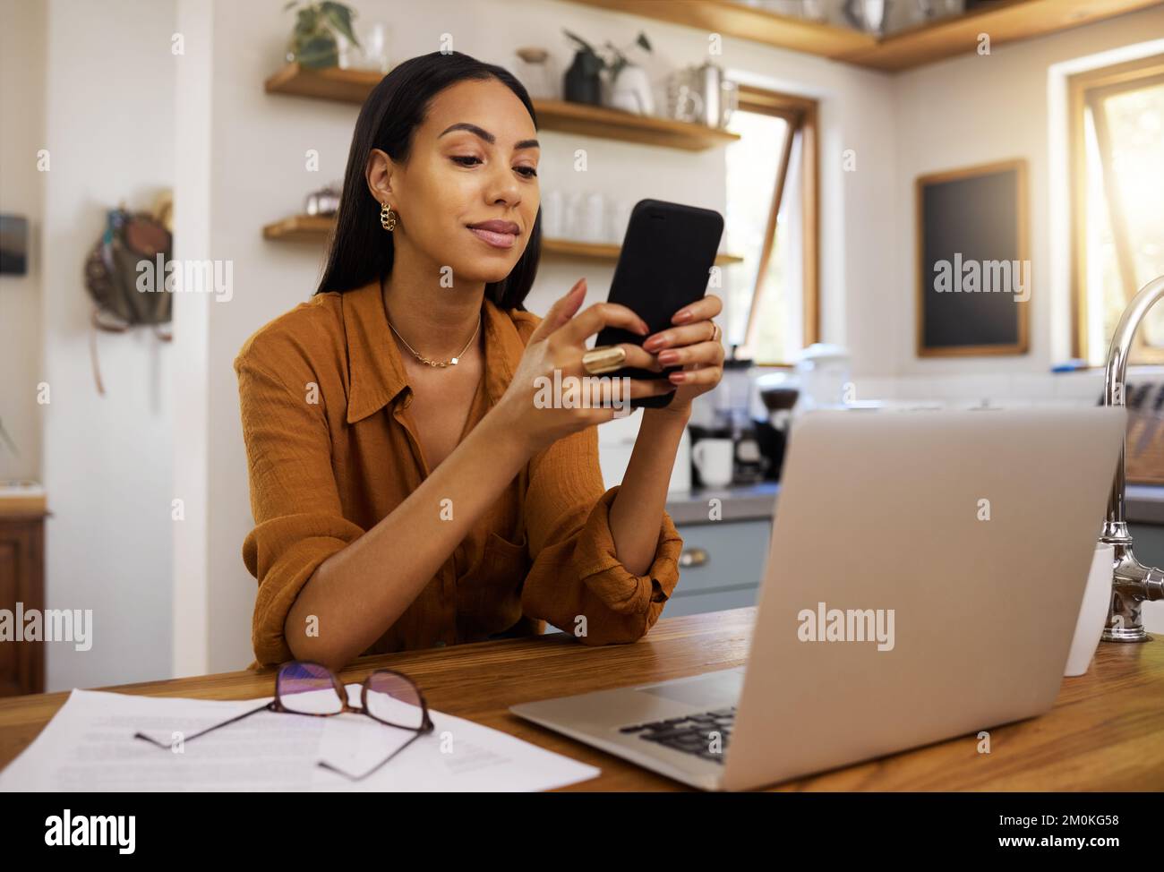 Young mixed race woman drinking a cup of coffee while using her phone ...