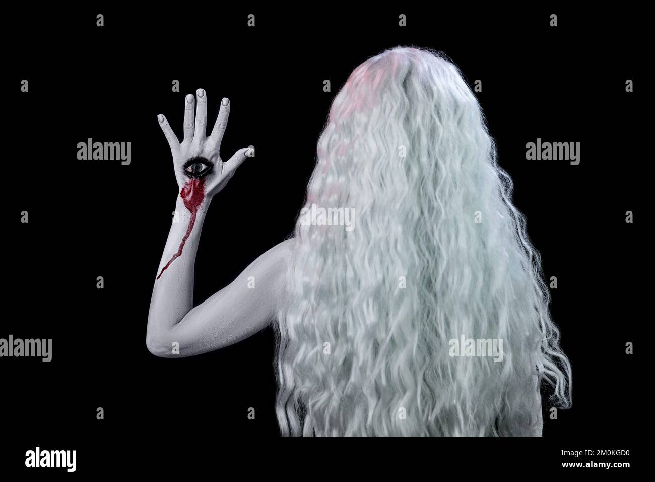 A woman in a white wig and an eye on her hand stands with her back on a ...