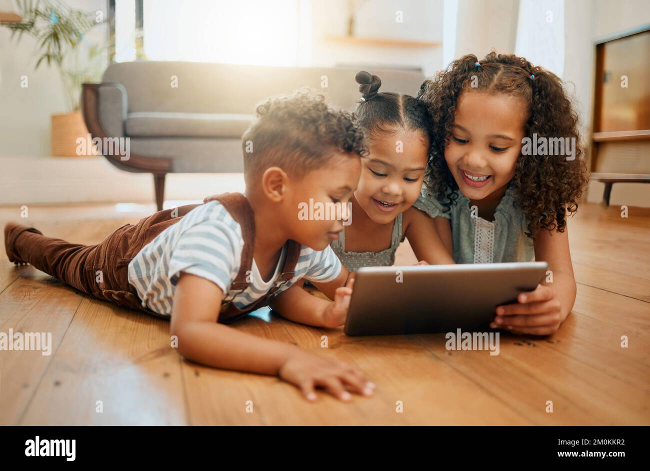 Three happy mixed race siblings relaxing on the lounge floor together ...