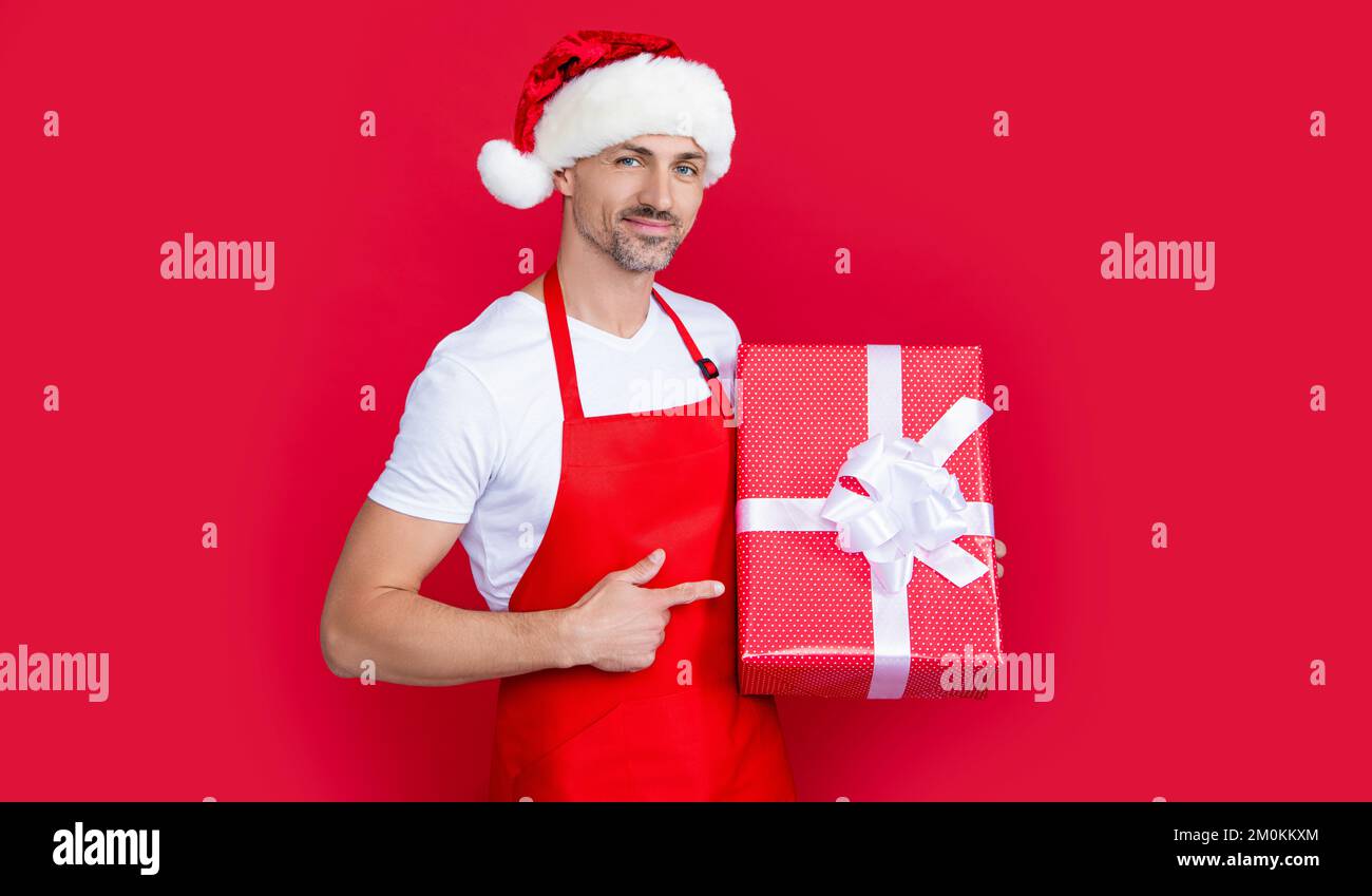 positive mature man in santa hat and red apron hold present Stock Photo ...