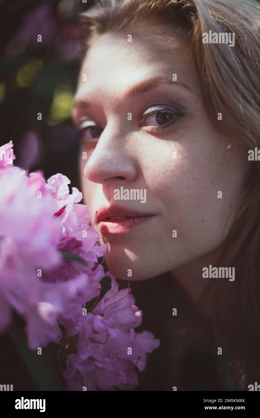 Close up lady pressing cheek against shrub with pink flowers portrait ...