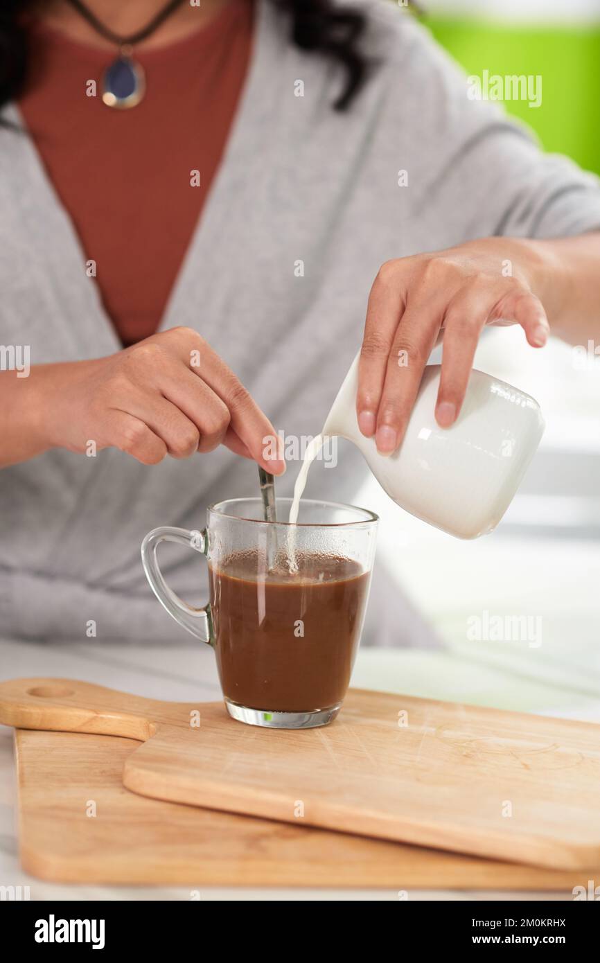 Closeup image of woman adding milk in morning coffee and mixing with ...