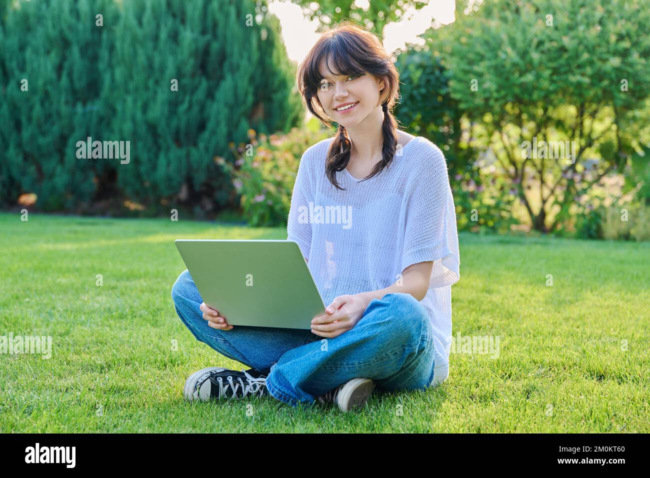 Teenage girl sitting on grass using laptop, looking at camera Stock ...
