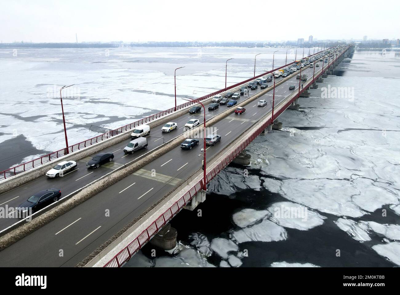 Many cars drive over river bridge in winter. Traffic jam, air pollution ...