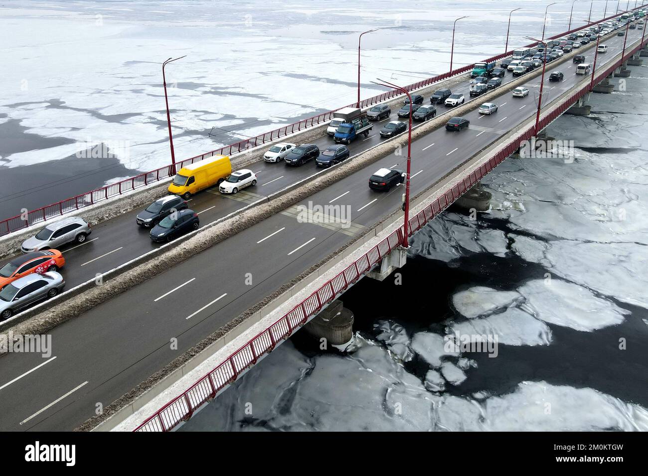 Many cars drive over river bridge in winter. Traffic jam, air pollution ...