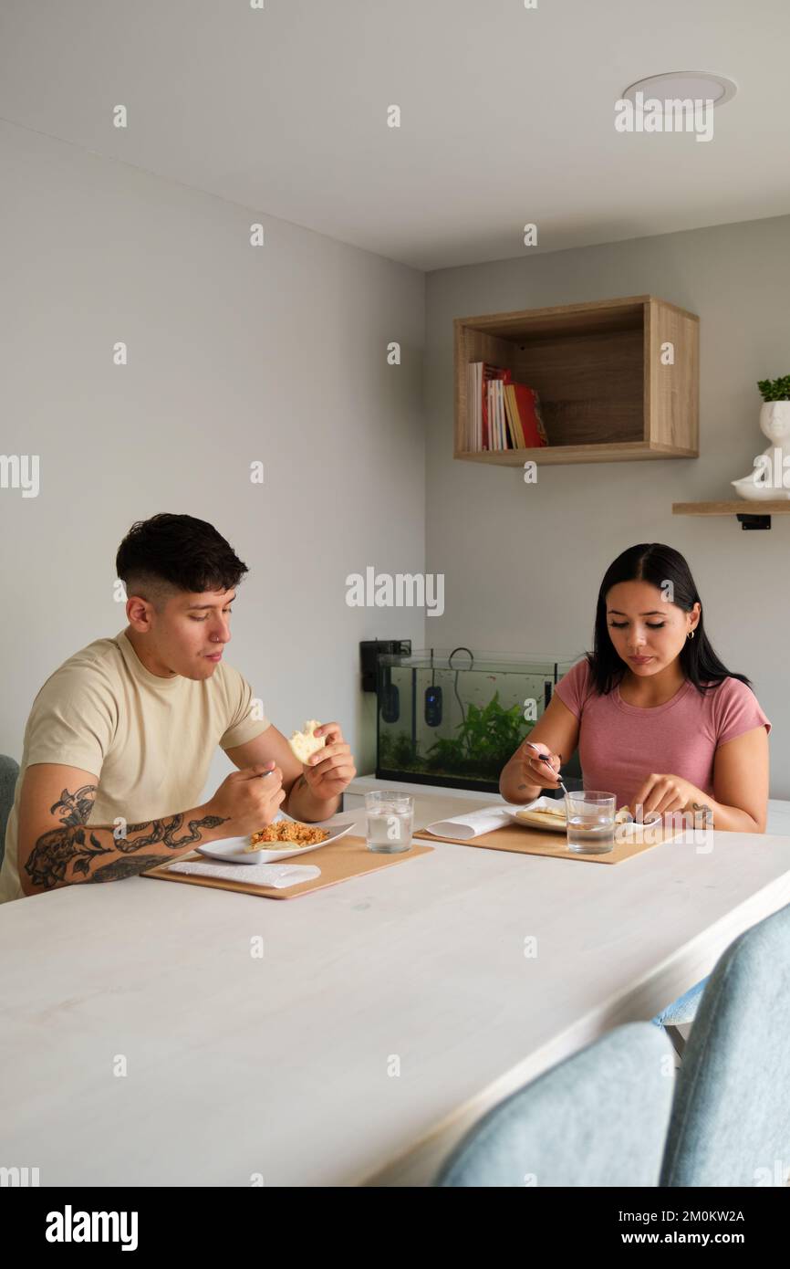 Two young latin people eating traditional arepas in the living room ...