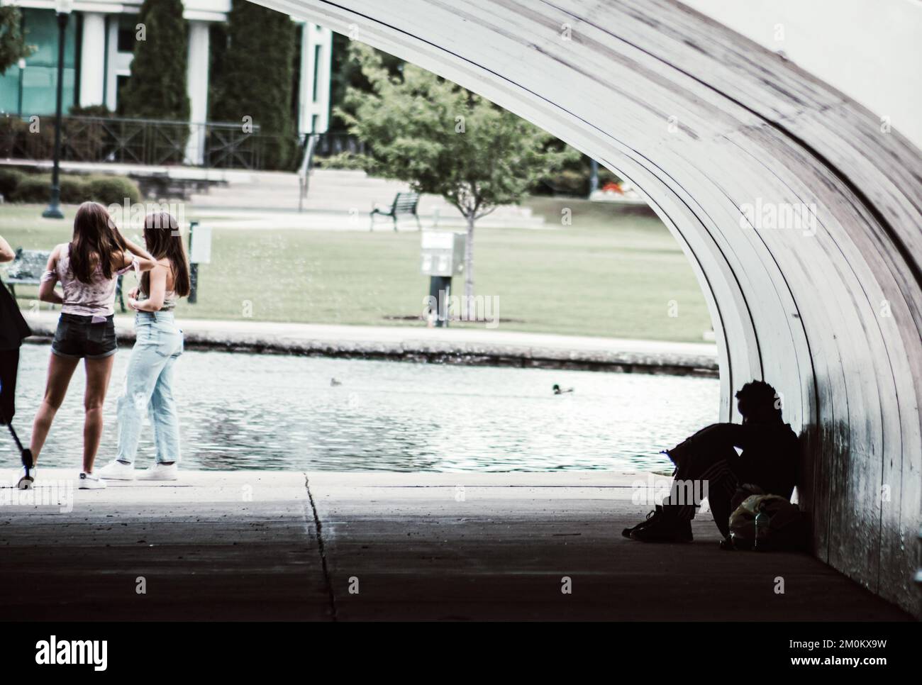 A silhouette of a poor man sitting under a bridge being ignored by ...