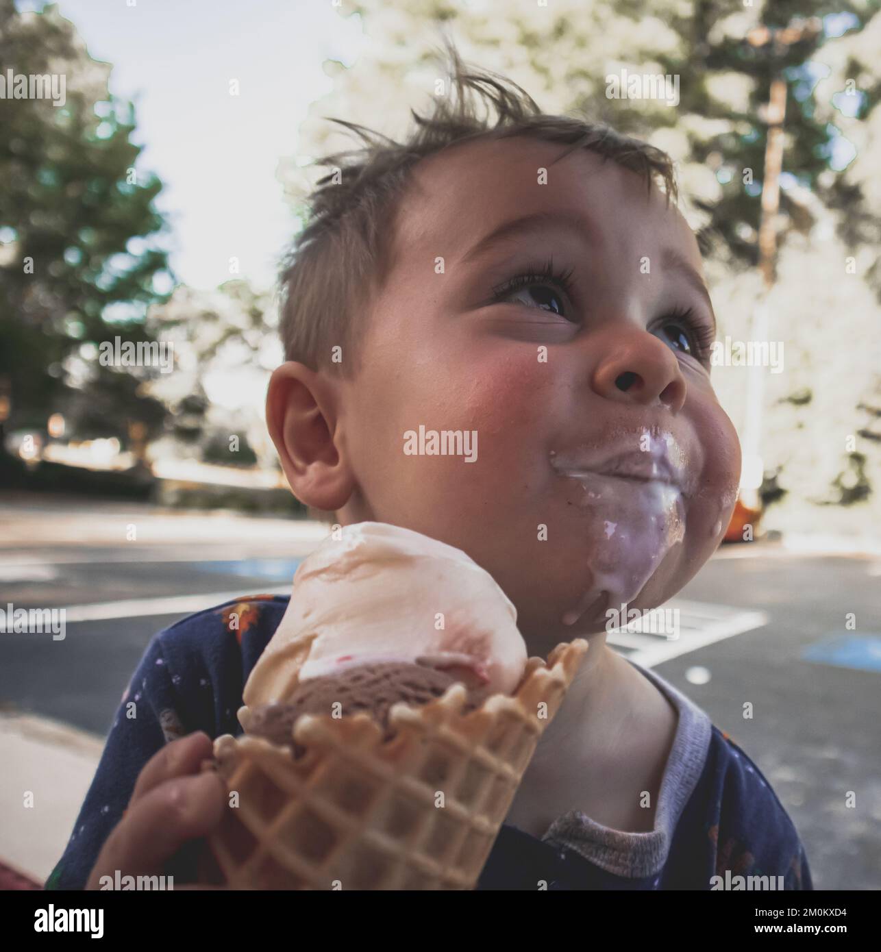 A closeup of a young boy eating a melting ice cream cone outside with ...