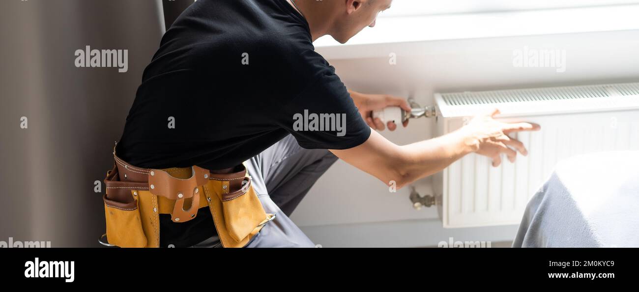 young man plumber checking radiator while installing heating system in ...