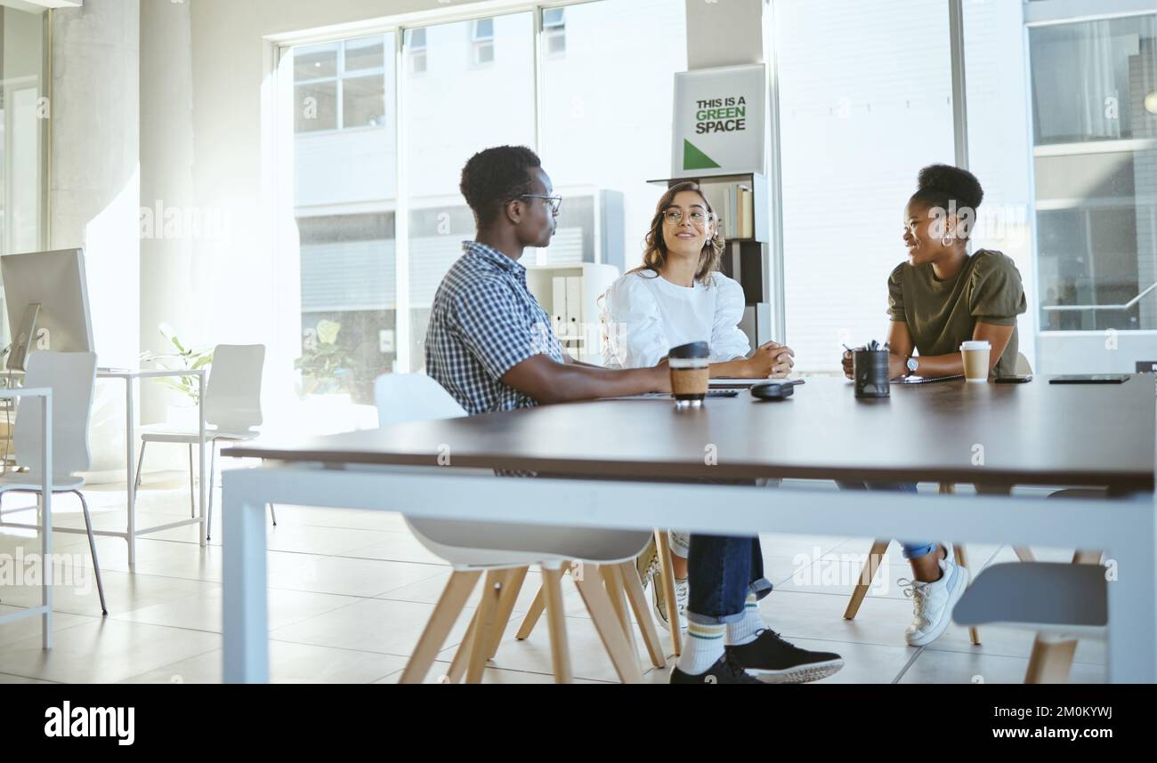 Three young happy businesspeople having a meeting while sitting at a ...