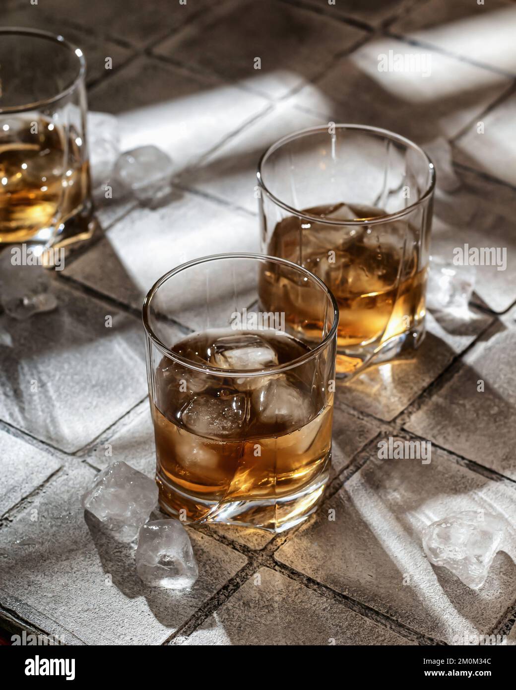 Whiskey with ice in glasses. Gray tile background. Hard light, copy ...