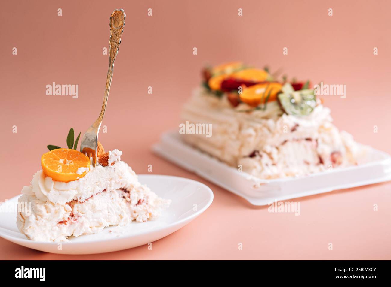 Festive meringue roll cut on round plate with fork on pink background ...