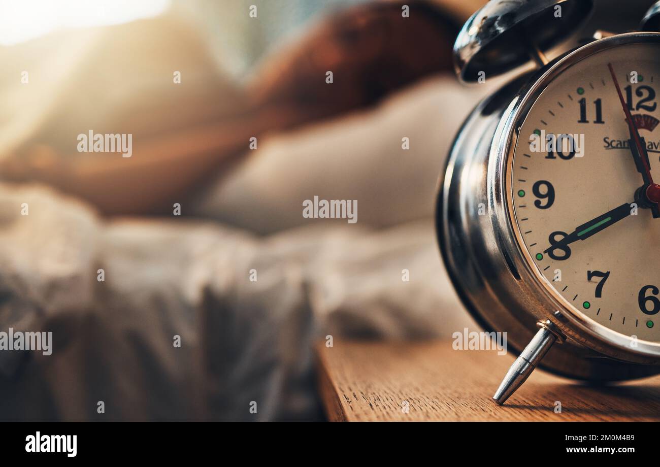 One young mixed race woman resting in bed before her alarm clock sounds ...
