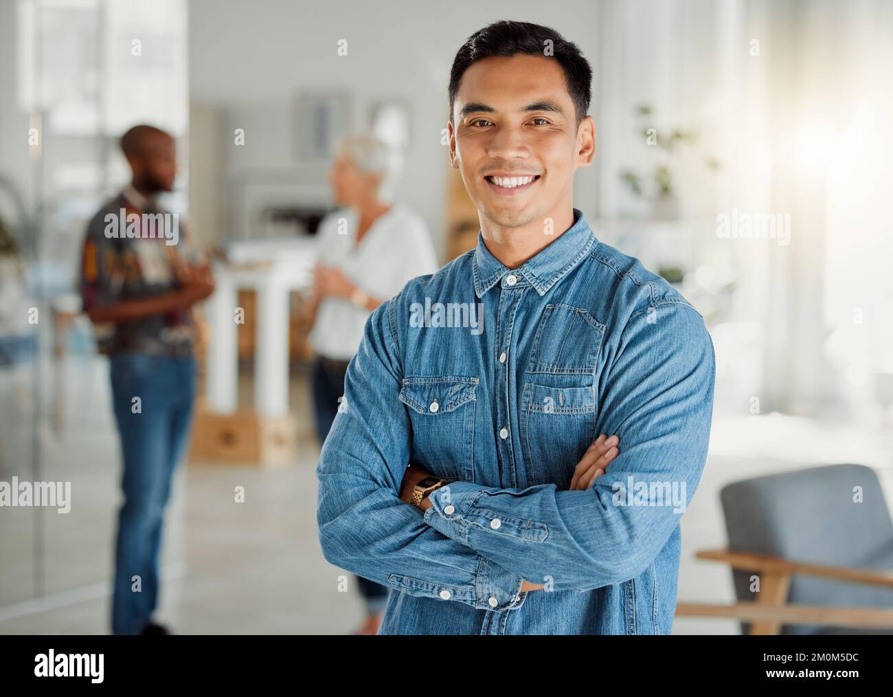 Portrait of a happy asian businessman standing with his arms crossed at ...