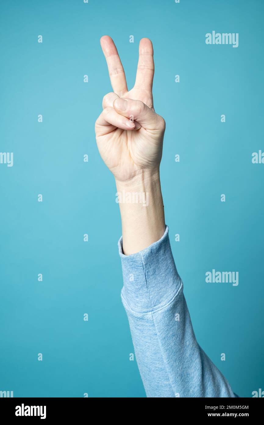 Victory sign, two fingers up, on a blue background Stock Photo - Alamy