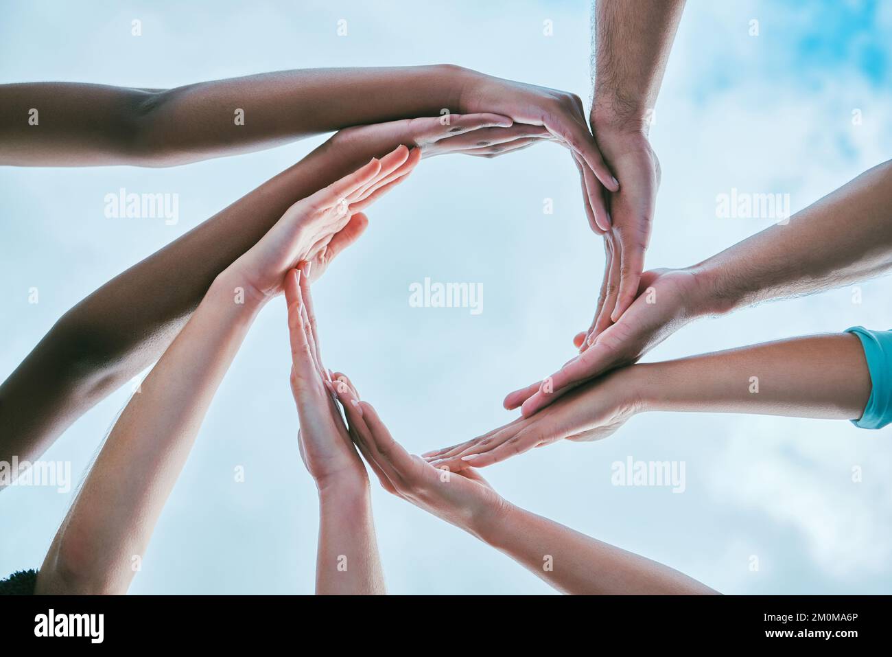 Closeup of diverse group of people from below joining hands together to ...