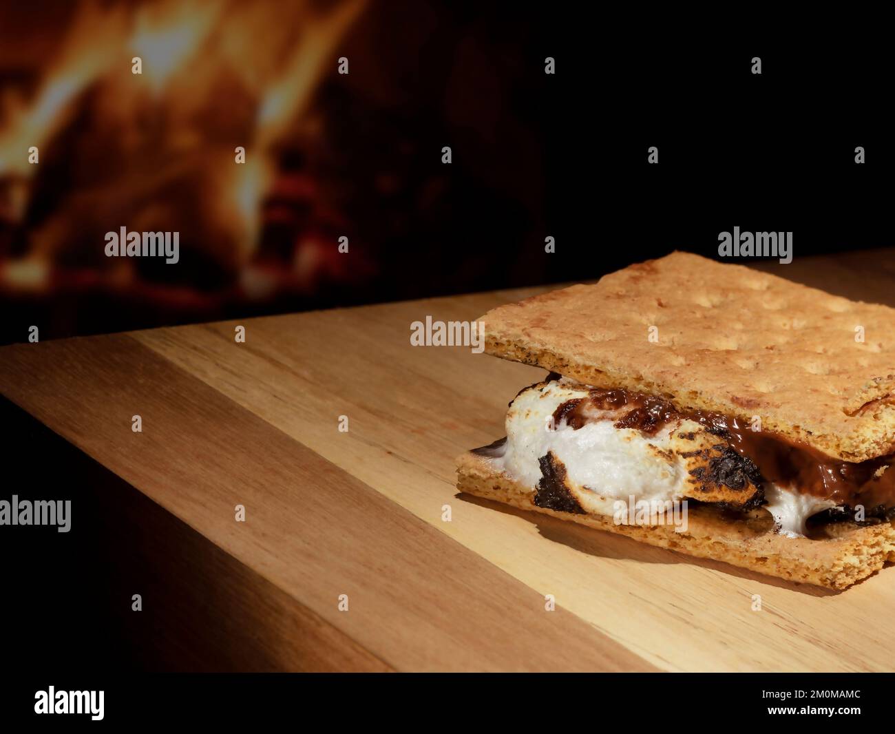 Smore on a wood surface with a campfire behind Stock Photo - Alamy