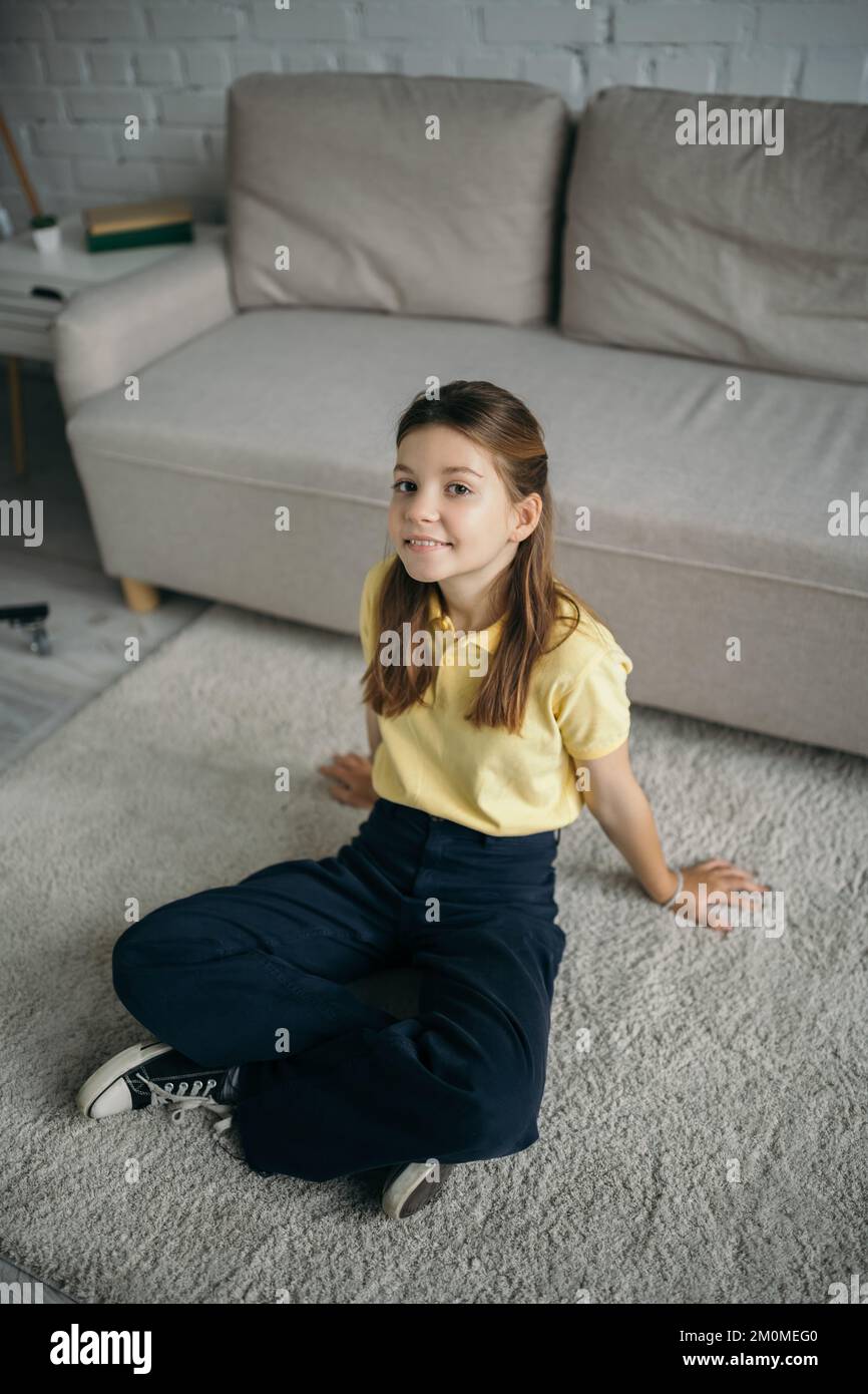 high angle view of happy girl sitting on floor with crossed legs near ...
