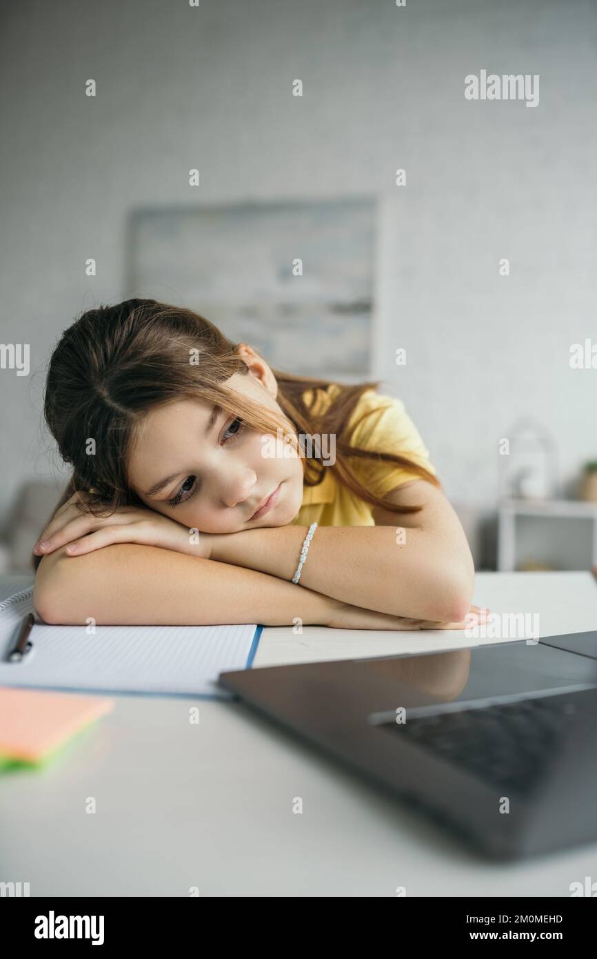 tired girl lying on table near notebook and laptop with blank screen at ...