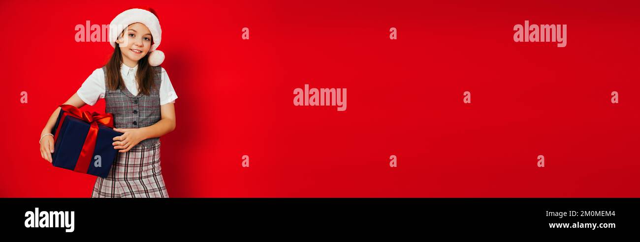 preteen girl in santa hat holding new year present and smiling at ...