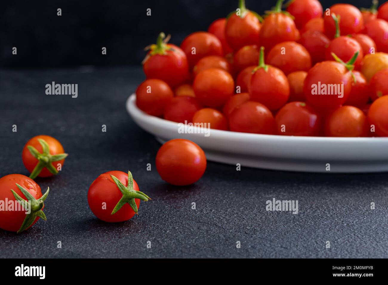 Red cherry tomatoes in a light dish on a dark background, vegetarian ...