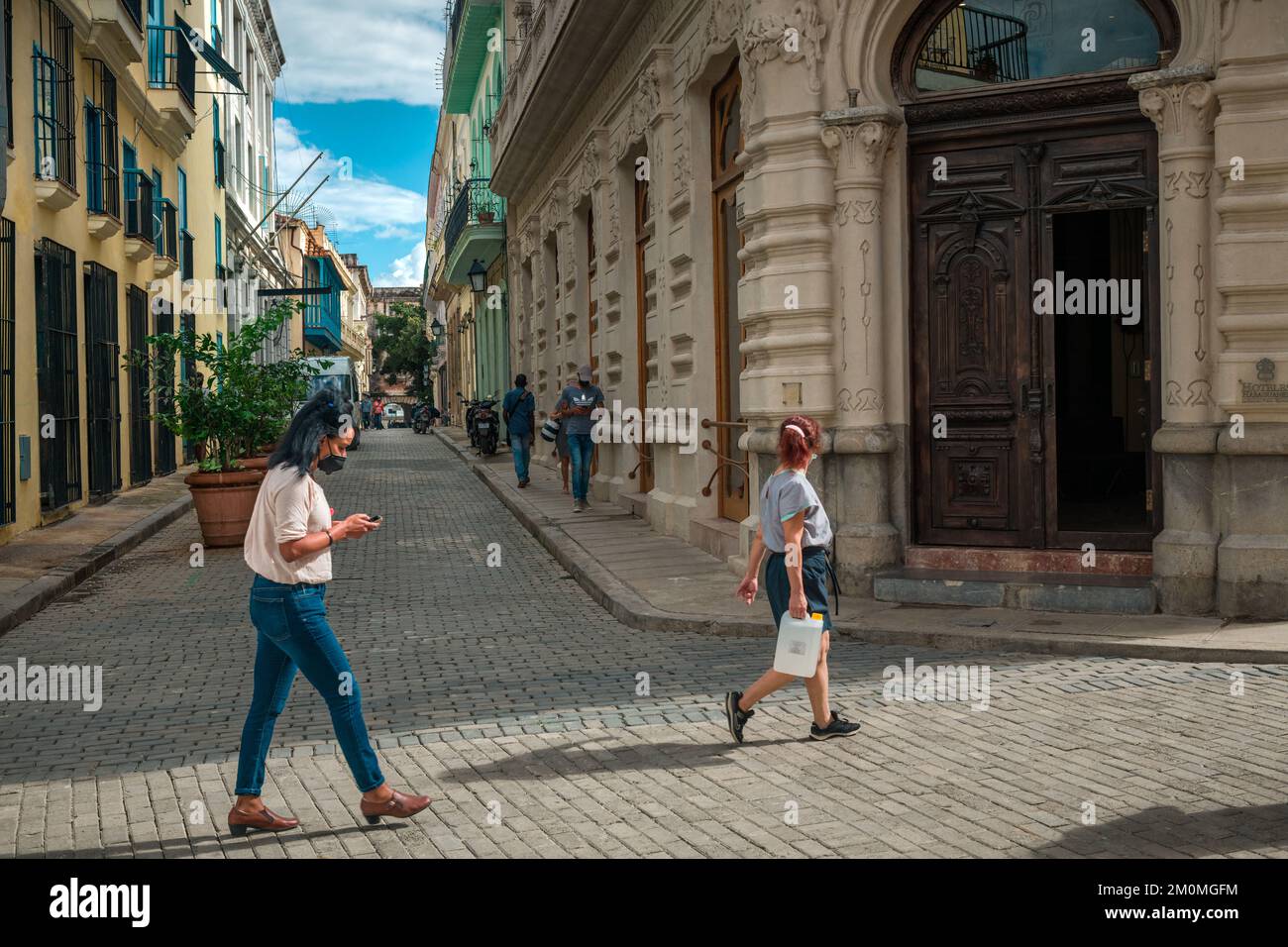 Cuban Latin people walking on Havana next restored old buildings the sun on the bodies of two ...