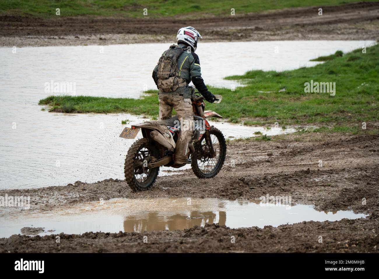 motorcyclist taking an off road bike across mud and waterlogged terrain ...