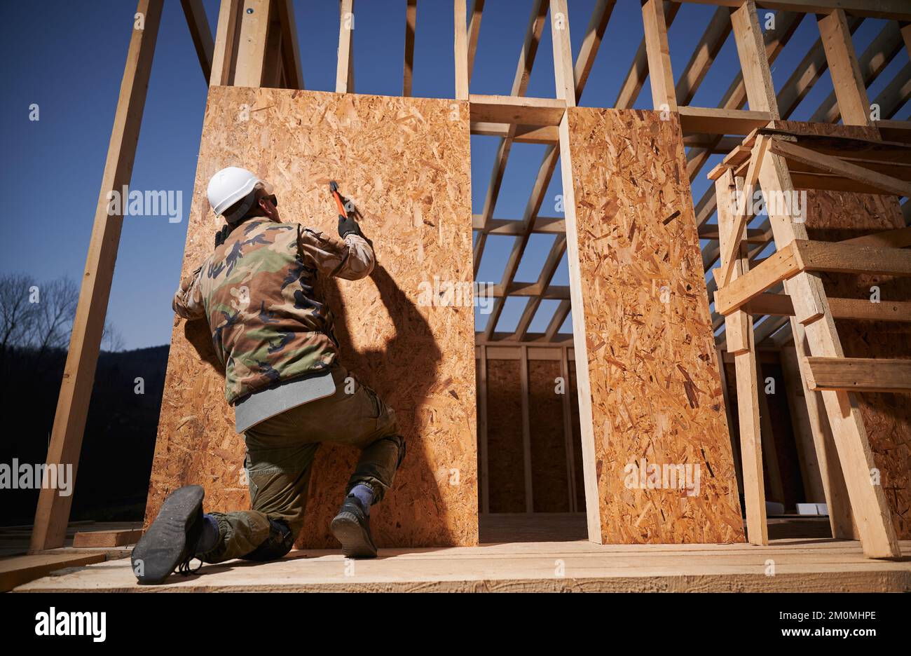 Carpenter hammering nail into OSB panel on the wall of future cottage ...